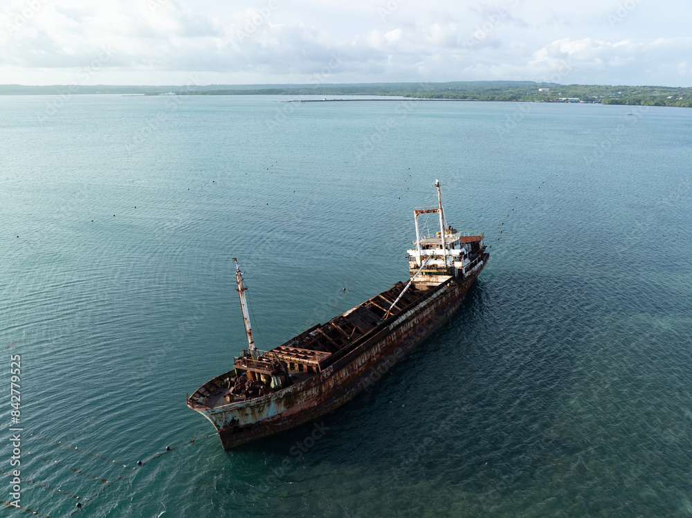 An old, rusted shipwreck has floundered in shallow water in the harbor ...