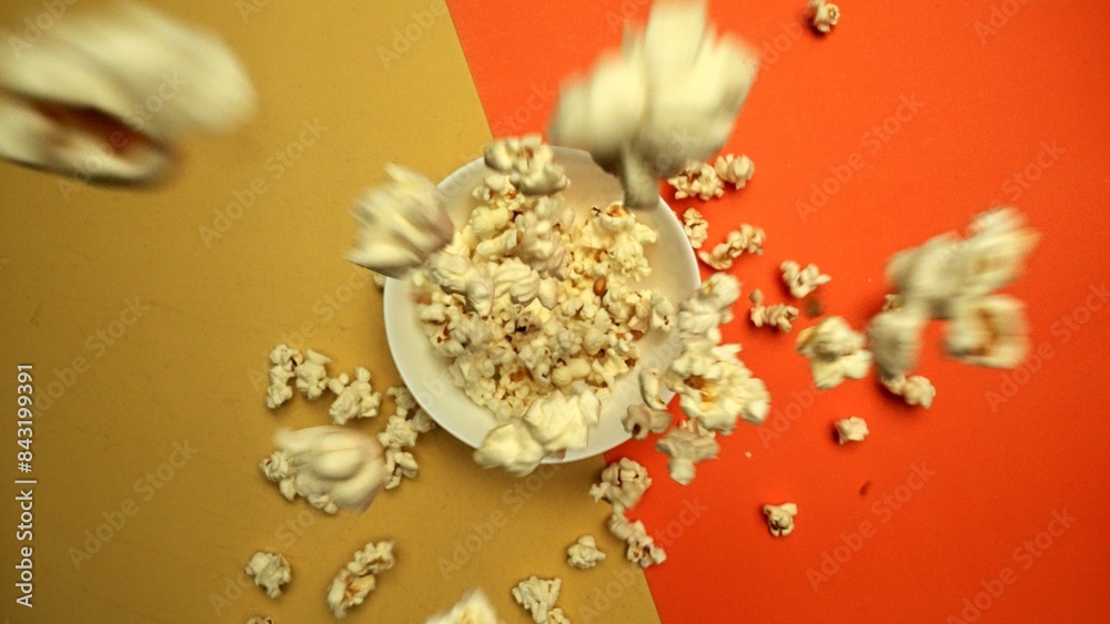 Top down view of flying popcorn dropping at white bowl with yellow and ...