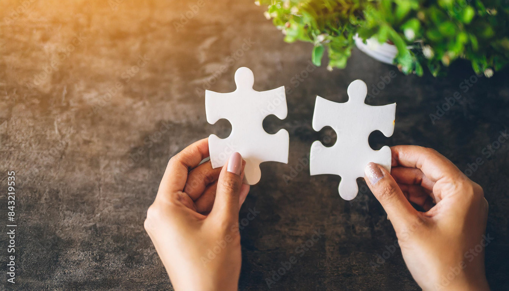 Two hands each holding a jigsaw puzzle piece, aligning them against a ...
