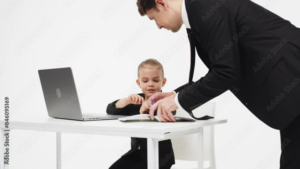 A business little girl in a stylish formal suit signs papers at her ...