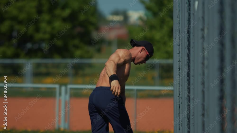 Bodybuilder in black cap and sunglasses is training on sports ground ...