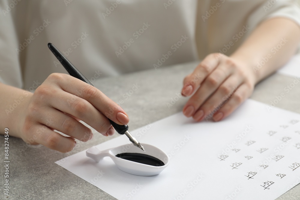 Calligraphy. Woman dipping fountain pen into inkwell at grey table ...
