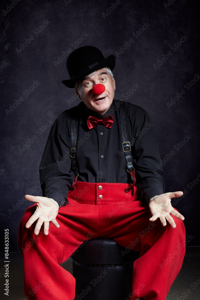 Clown on dark background. Dressed in red pants and a black shirt with ...