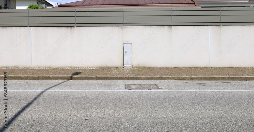 Utility box in the middle of a fence made of white plaster wall with ...