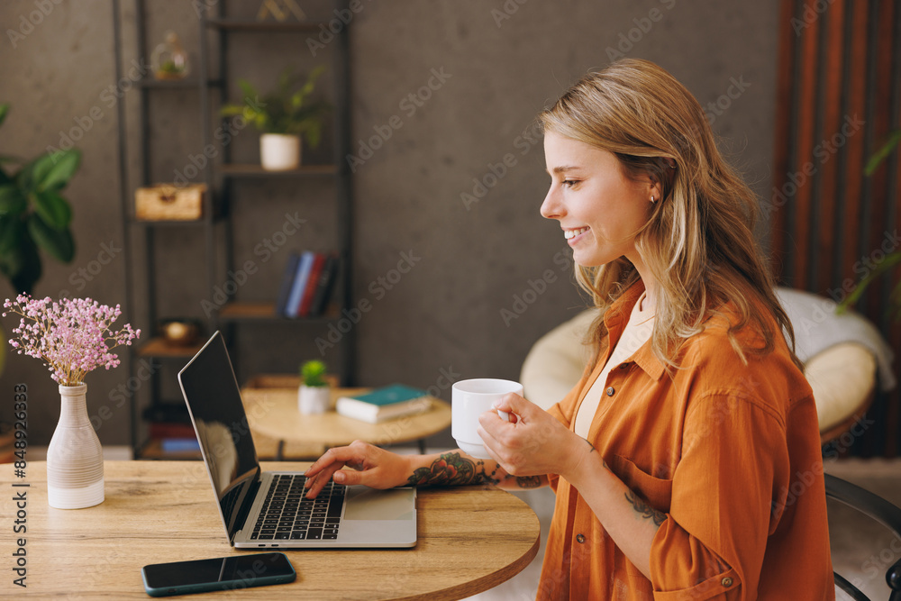 Foto de Side view young IT woman wearing orange shirt hold use laptop ...