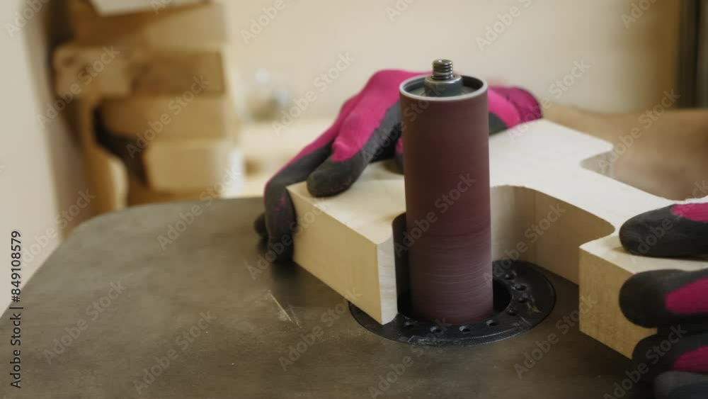 A gloved hand works with a wooden blank on a sanding machine. The ...