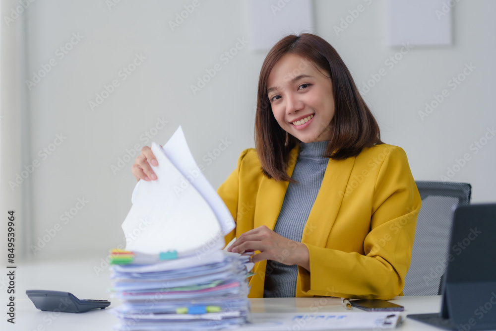 Smiling businesswoman sorting documents at her desk in office, wearing ...