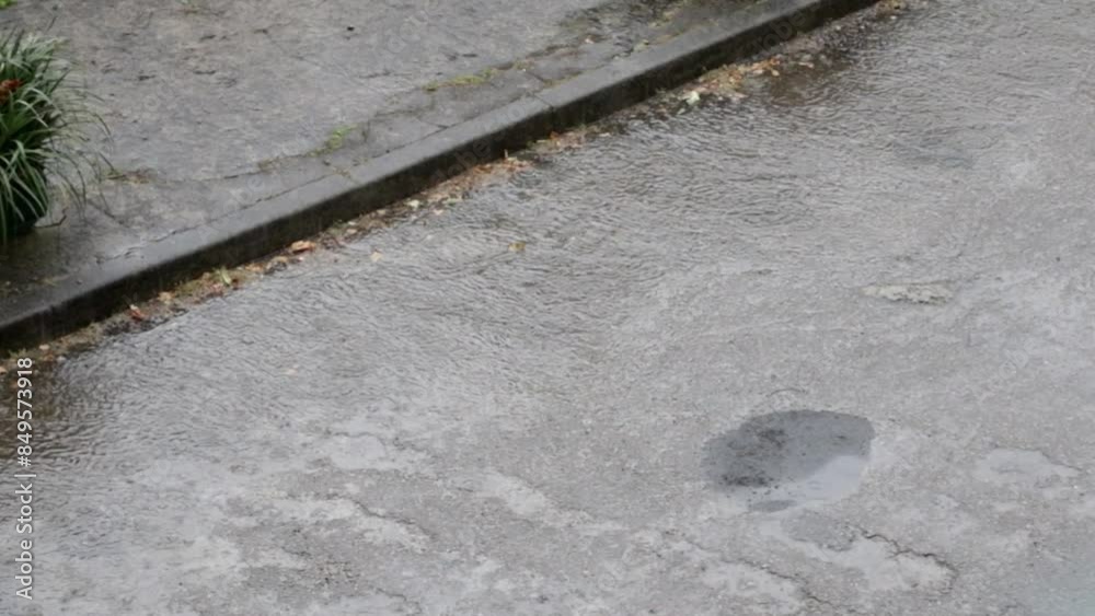 Rain falling on a city street, forming small puddles along the curb and ...