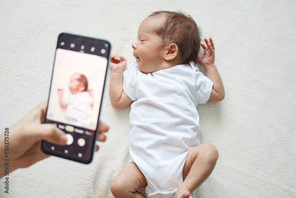 Mother shooting her newborn baby by smartphone lying on white sheet ...