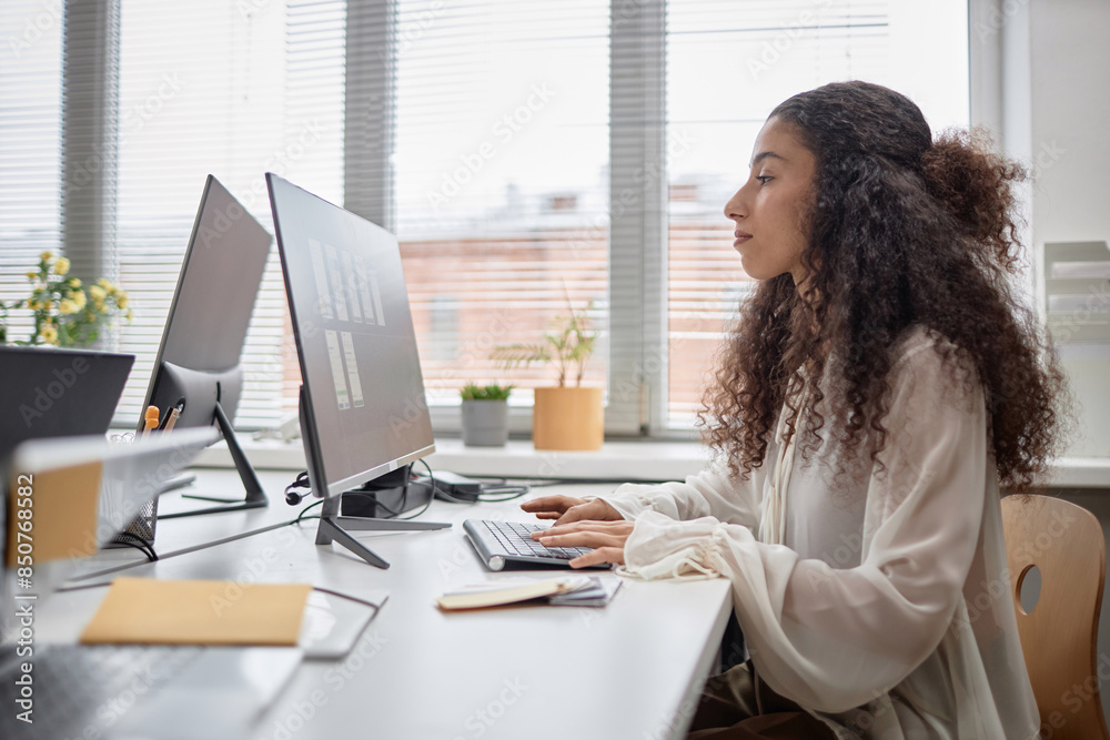 Side view portrait of Middle Eastern curly woman typing on keyboard at ...