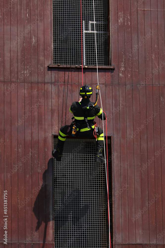 firefighter with helmet and uniform lowering himself down from the ...