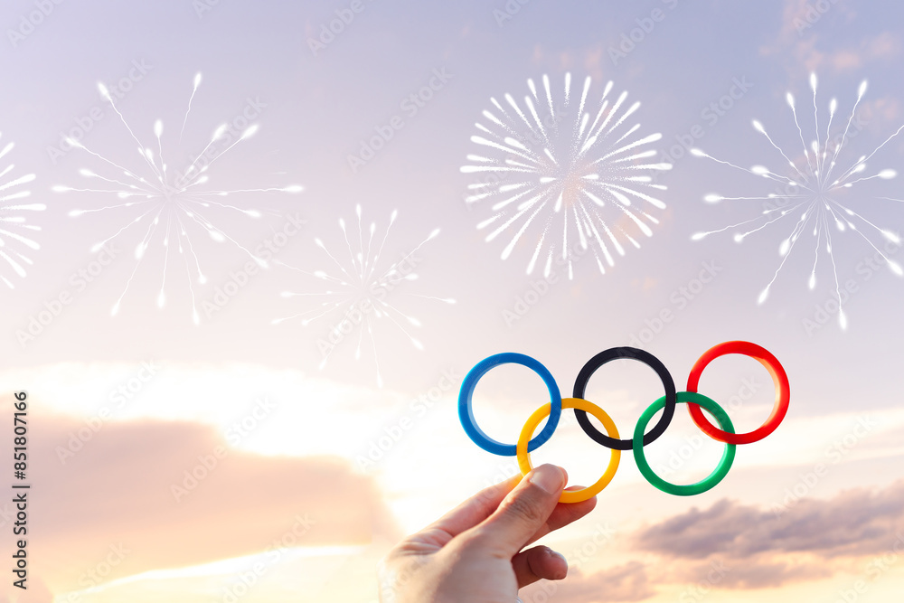 Hand holding Olympic rings against an evening sky, embellished with ...
