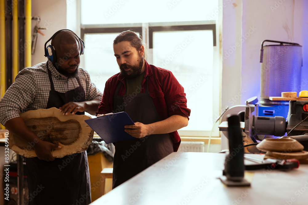 Cabinetmaker and apprentice looking over technical drawings on notepad ...
