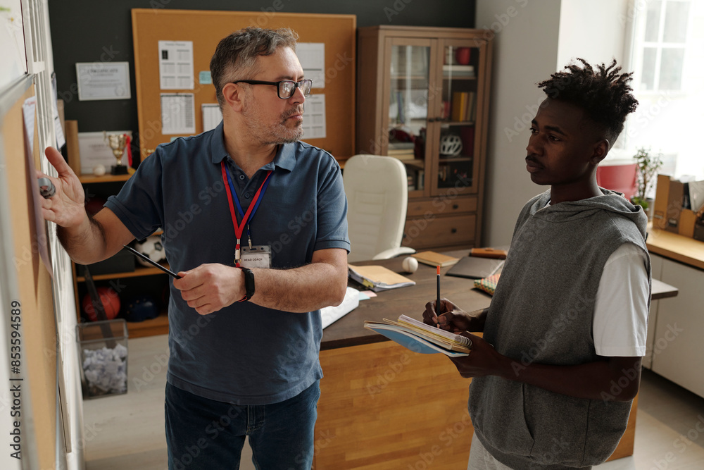 Coach explaining sports strategies to student on bulletin board at ...
