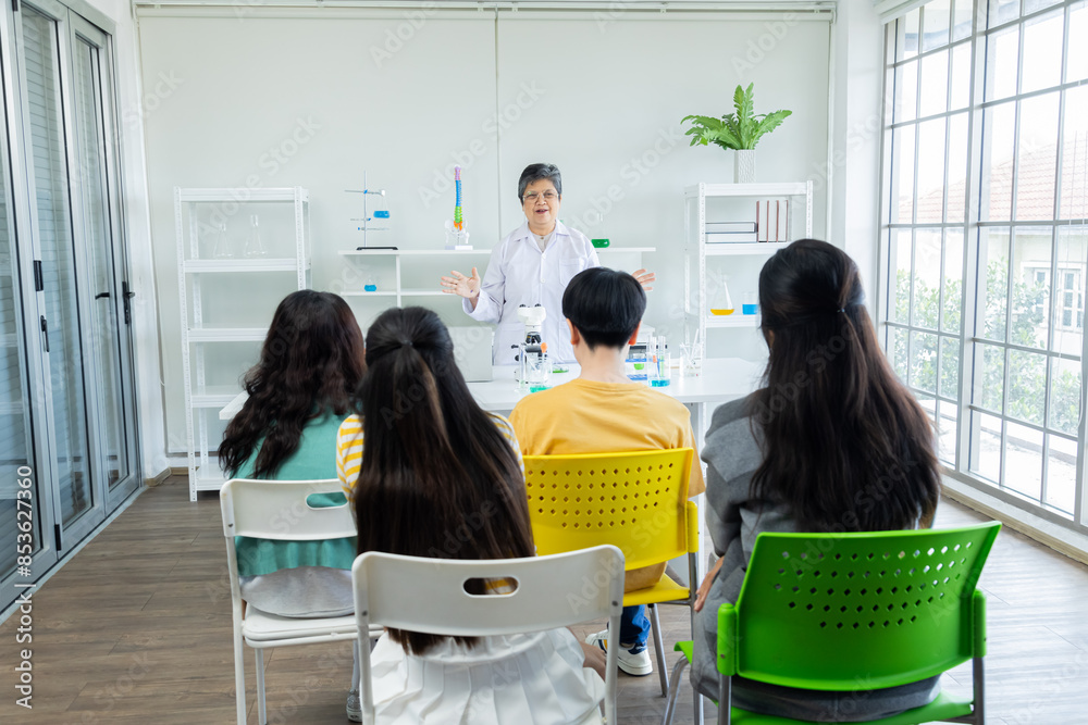 Senior teacher woman demonstrating microscope experiment to students in ...