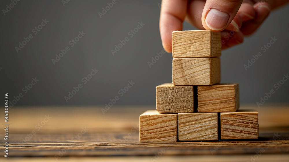 A hand carefully stacking wooden blocks, illustrating the concept of ...