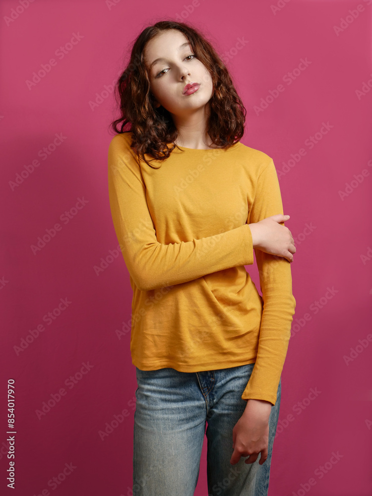Teenager girl in yellow shirt posing in a studio, red background. The ...