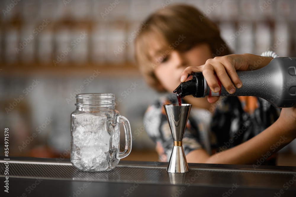 Little boy prepares a fruit cocktail with ice. He pours brown syrup ...