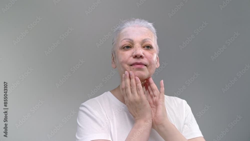Positive old woman massages forehead and cheeks spreading lotion on ...