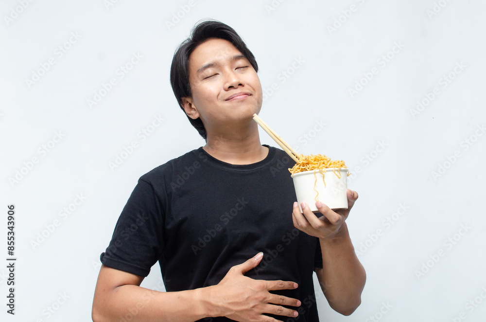 young asian man holding instant noodles and rubbing his belly with the ...