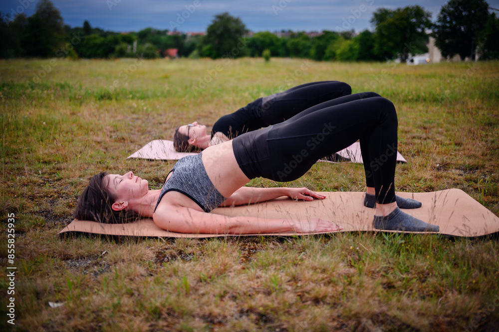 Two women in athletic wear practice the Bridge pose on yoga mats in a ...