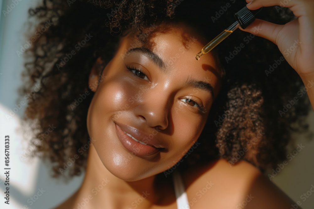 A joyful woman with curly hair applying skincare oil to her forehead ...