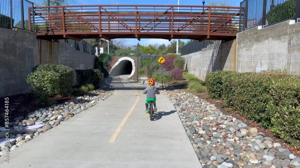 Little boy riding bicycle under a pedestrian walkway and through a ...