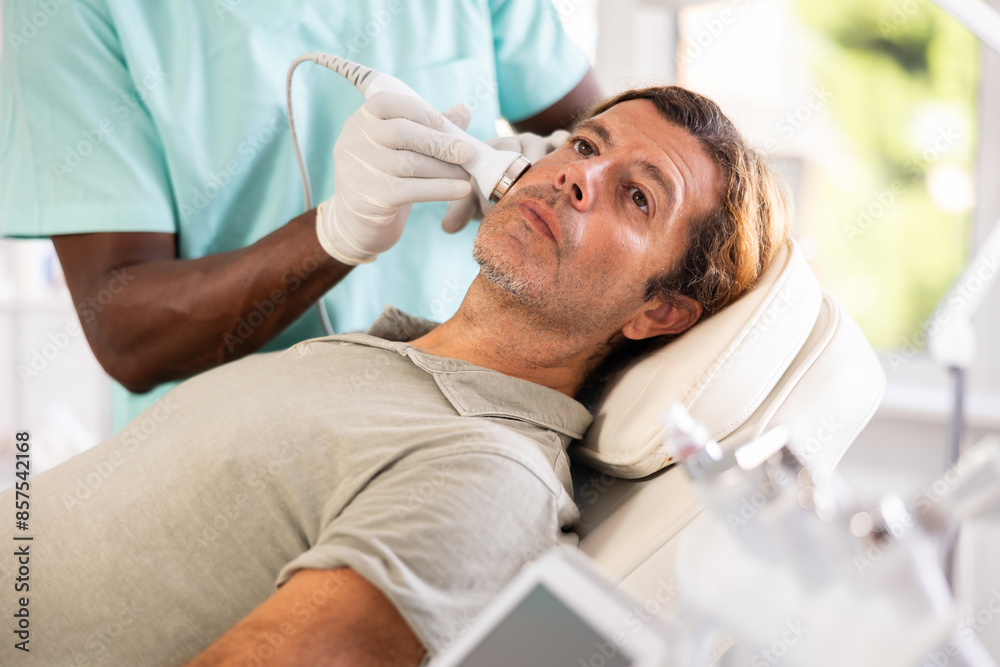 Adult man undergoing device-driven cosmetic facial treatment using high ...
