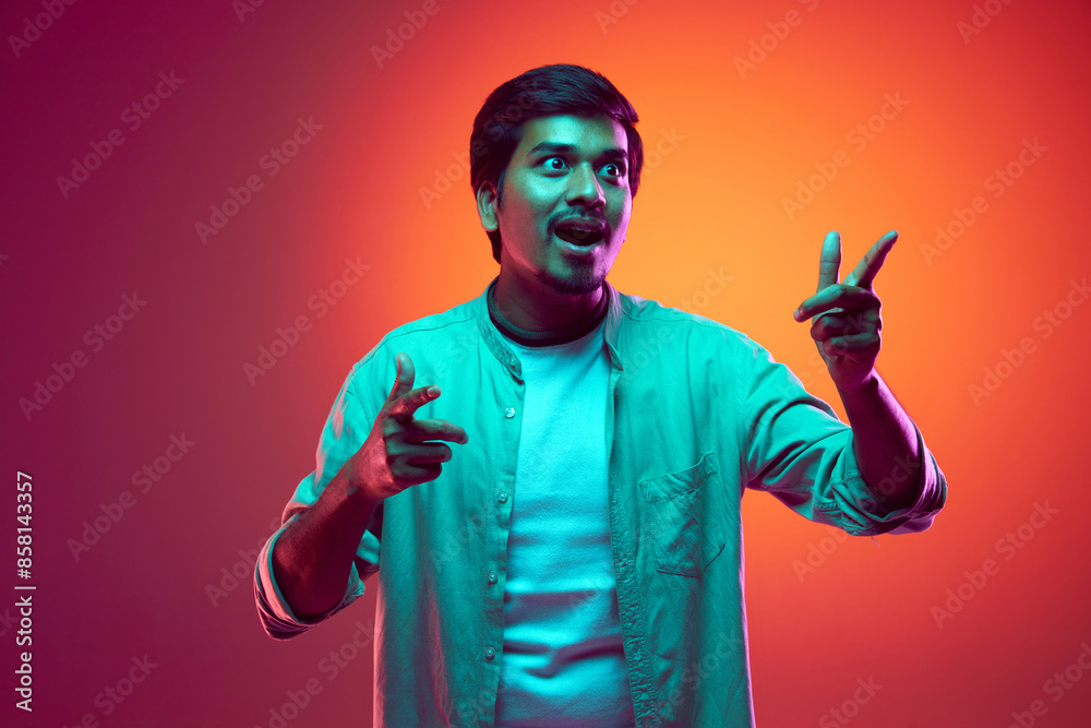 Excited young Indian man pointing at distance with shocked expression ...