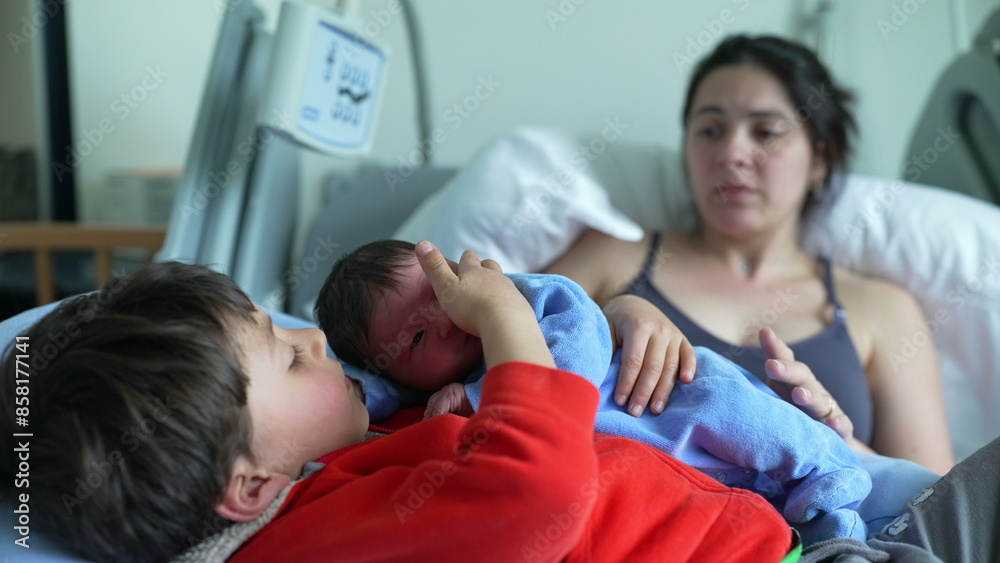 Older sibling lying on hospital bed with newborn baby, while mother ...
