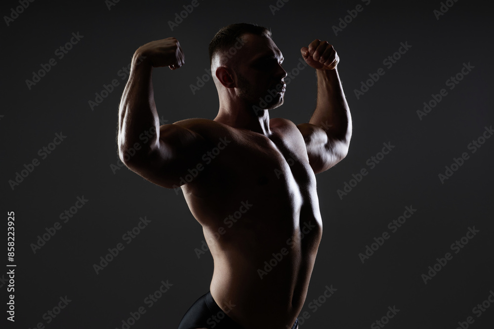 Medium shot of male bodybuilder in front double biceps pose contracting ...