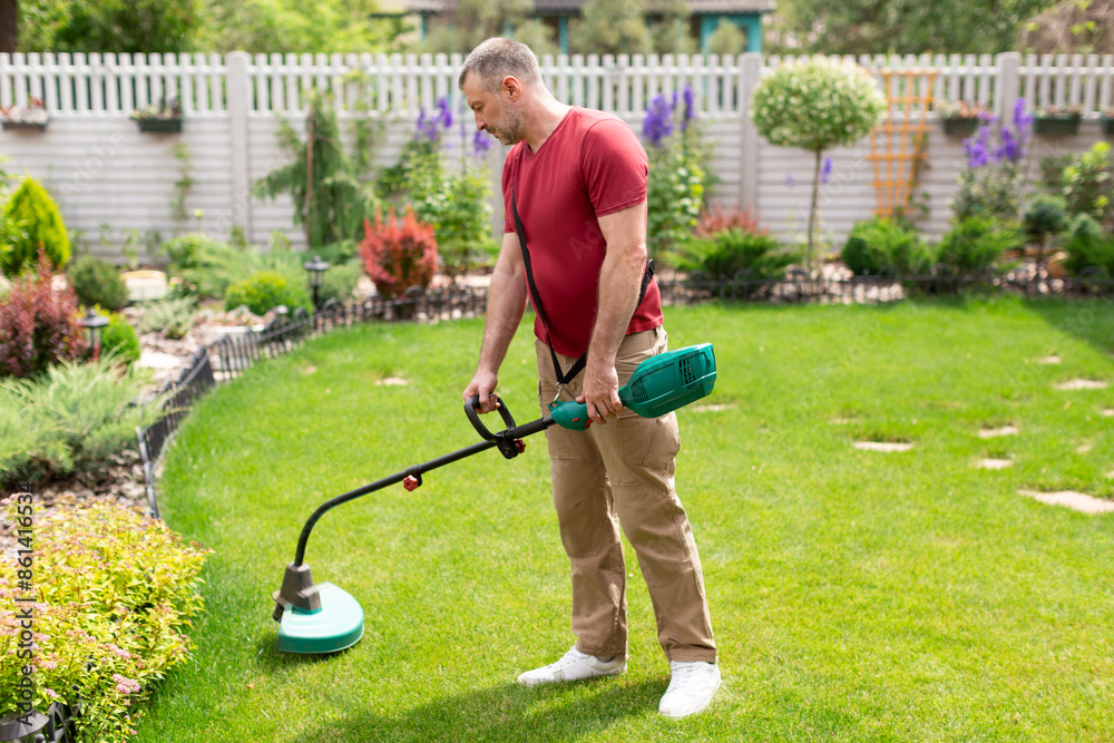 Man worker with string lawn trimmer mower cutting grass in his own ...