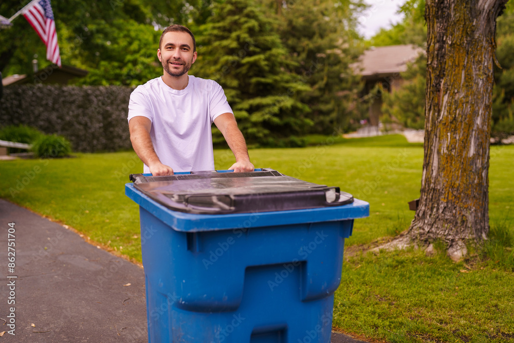 Young man pushes a large green plastic trash bin for weekly waste ...