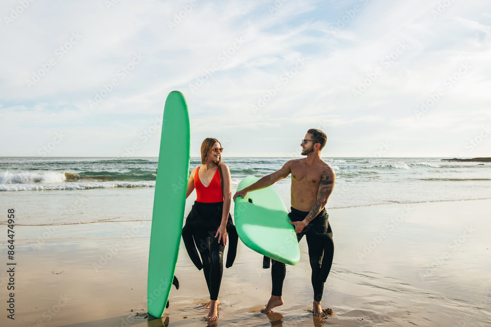 A young couple, dressed in swimwear and holding surfboards, are ...