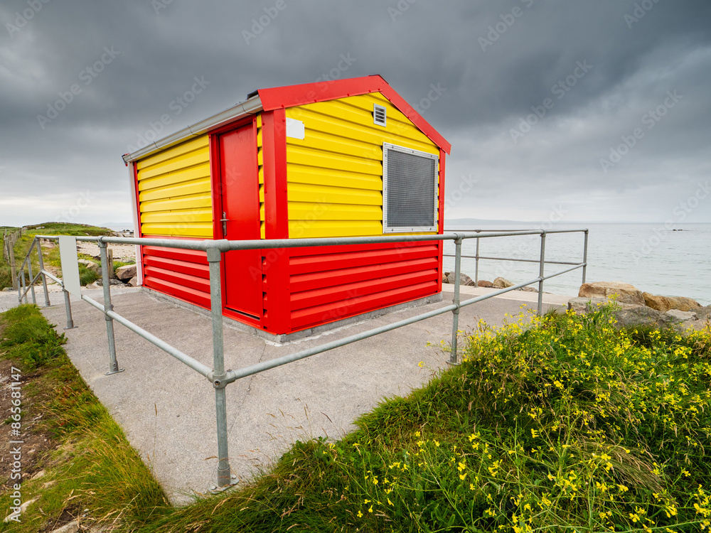 Red and yellow life guard hut on a green hill with metal hand rail ...