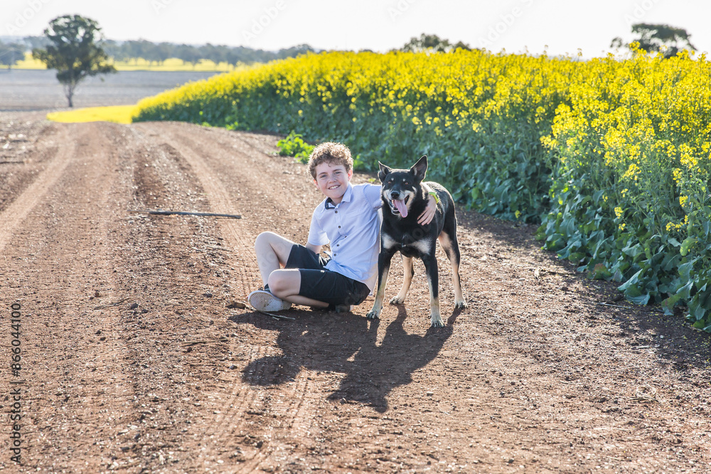 Tween boy sitting on dirt road on farm with arm around kelpie dog near ...