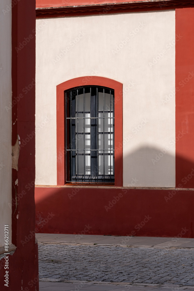 red arched window with black security bars on a white wall, reflecting ...