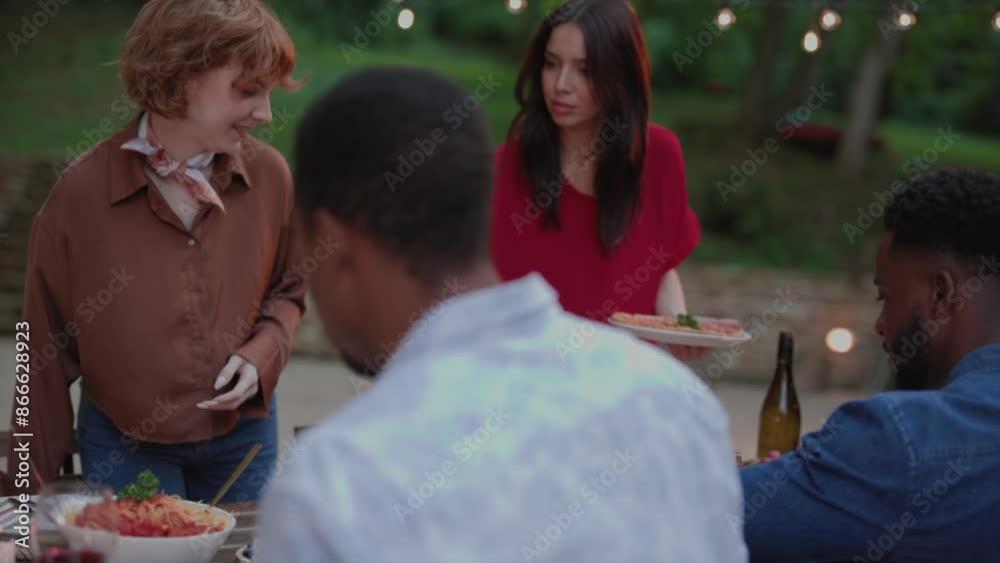 A multiracial group of friends in their 20s enjoying an outdoor dinner ...