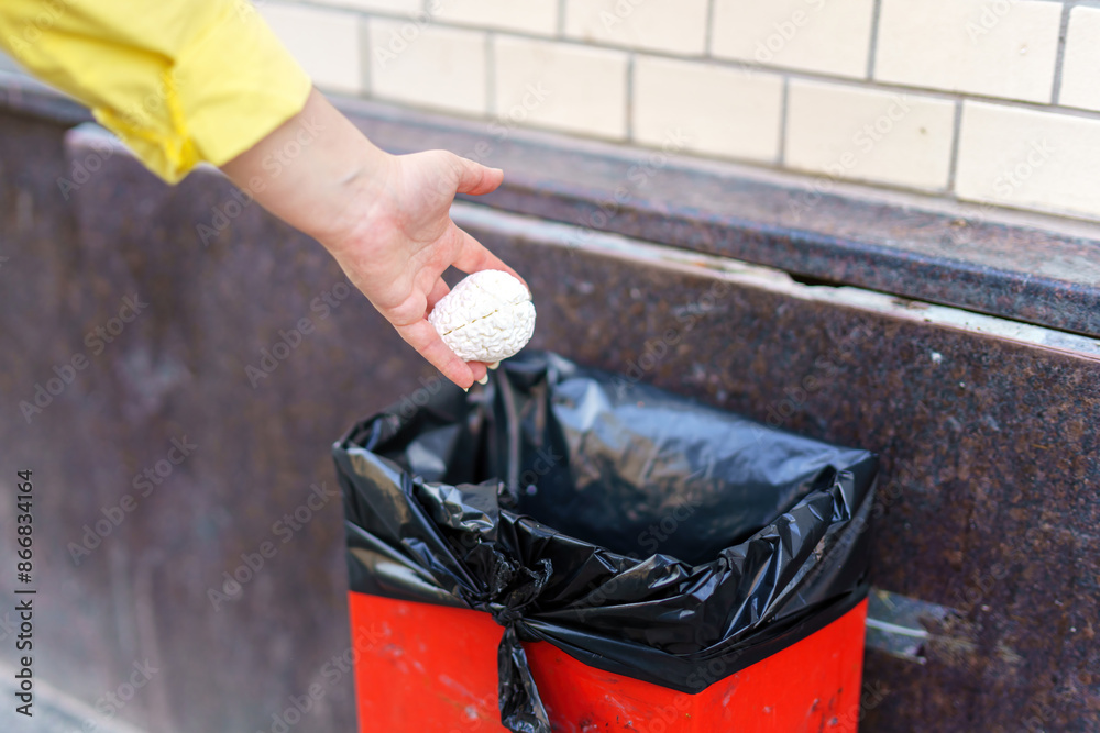 hand discarding a brain model into a trash bin, symbolizing the neglect ...