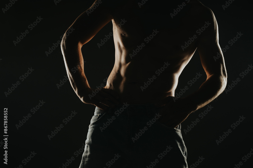 Silhouette of a shirtless man with a muscular build posing in a dark ...