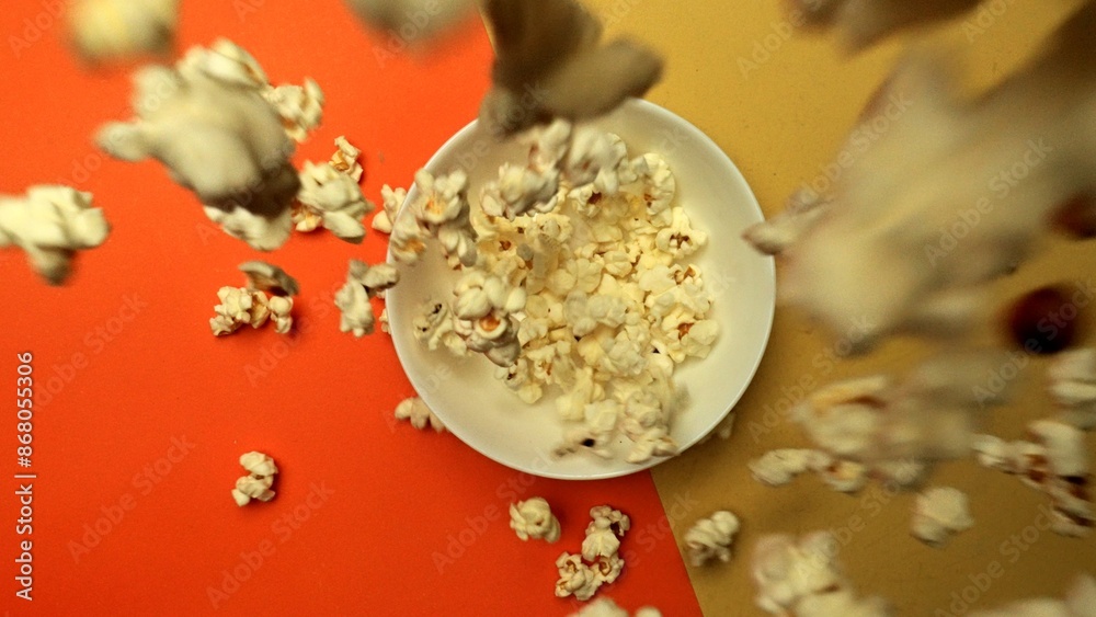 Top down view of flying popcorn dropping at white bowl with yellow and ...