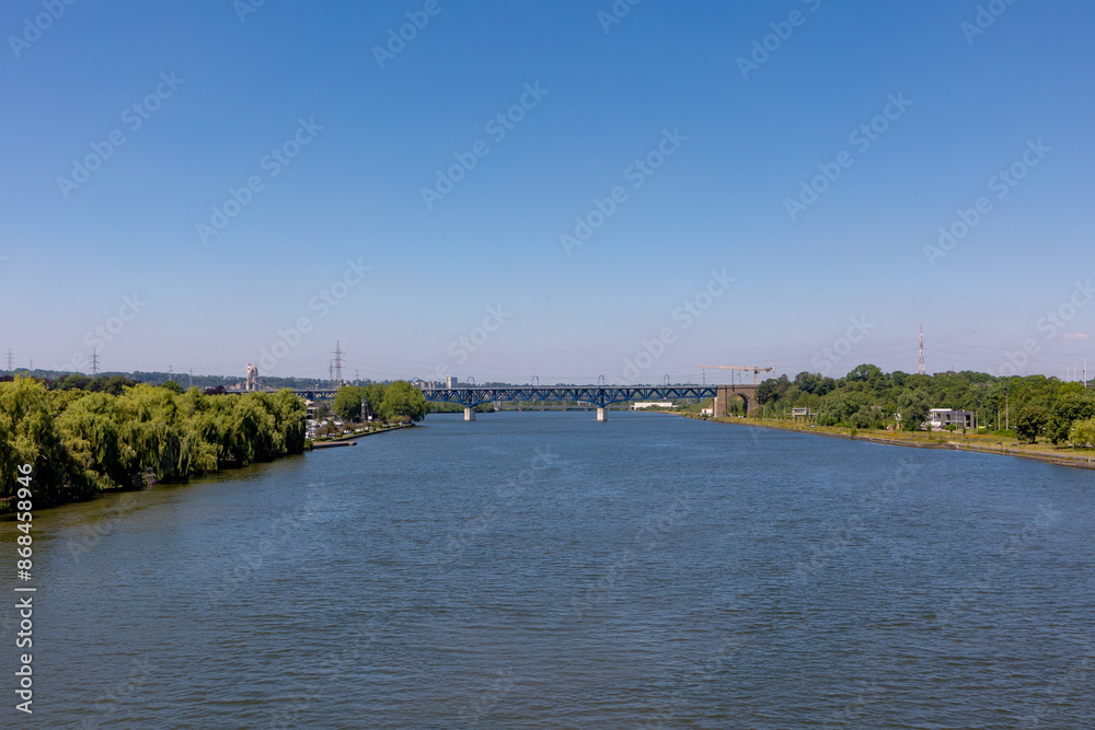 The Meuse river under blue sky in summer with small houses, tree and ...
