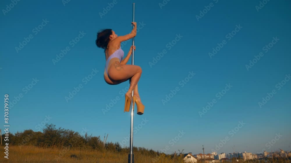 Woman gracefully pole dancing against a blue sky backdrop. Slow motion shooting. Pole dancer ...