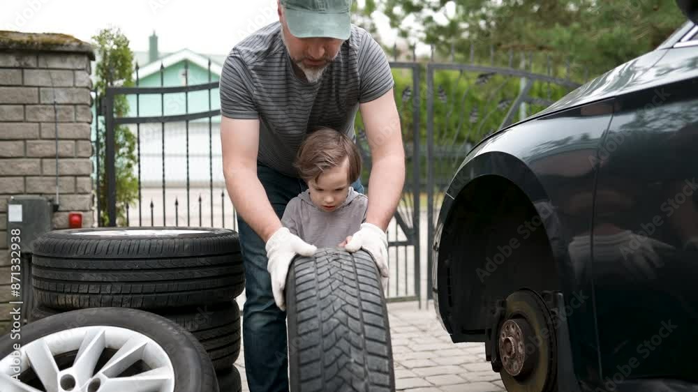 Cute toddler boy helping his father to change car wheels in their ...
