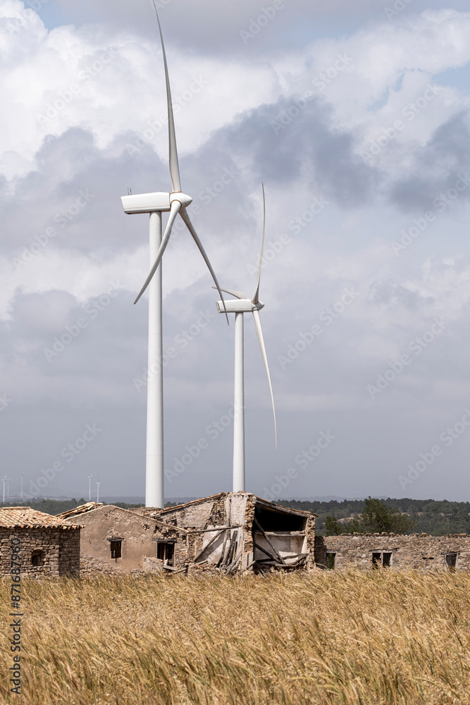 Foto de Wind turbines rise above abandoned rural buildings, juxtaposing ...