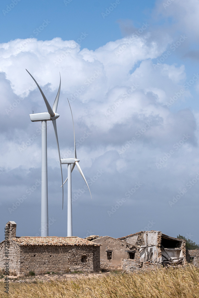 Two large wind turbines tower over old stone houses, juxtaposing modern ...