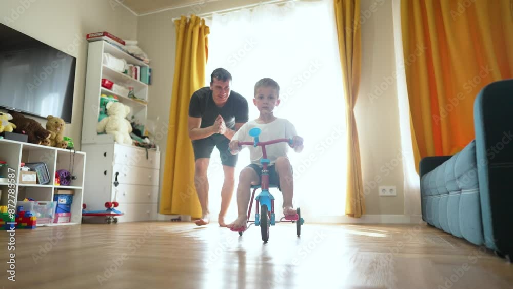 Father encouraging child on tricycle. boy riding tricycle indoors ...