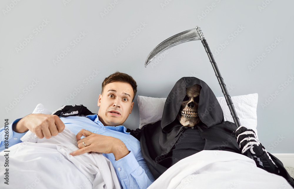 Foto de Shocked young scared man lying on bed in bedroom under blanket ...