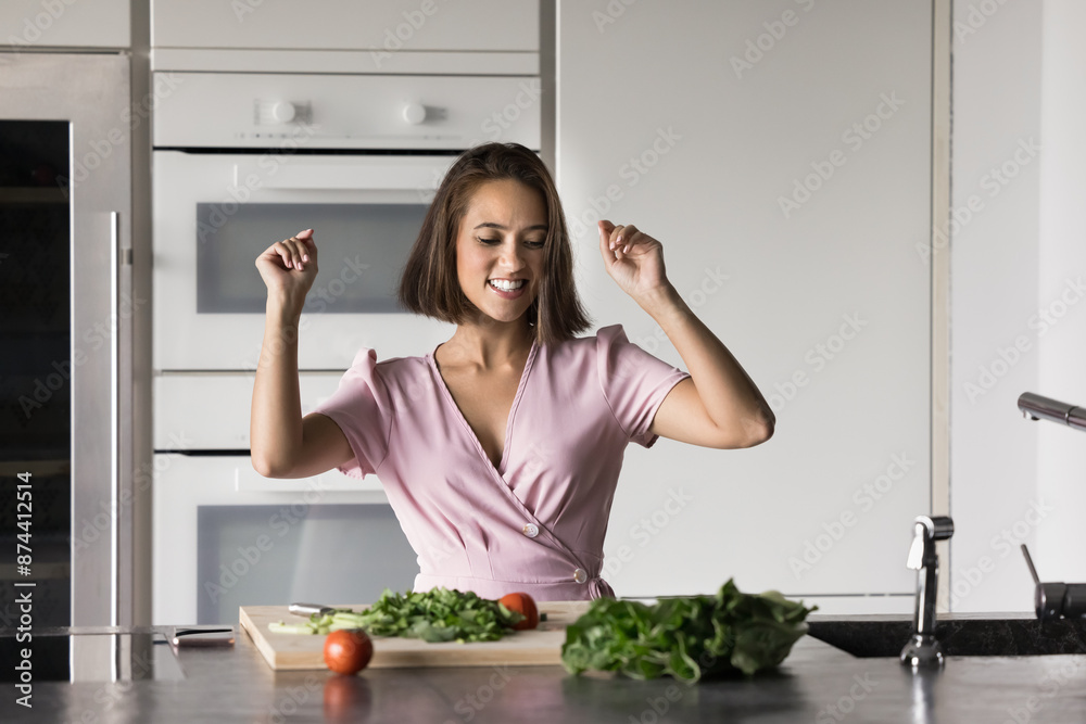 Excited beautiful active young woman dancing and cooking healthy dinner ...