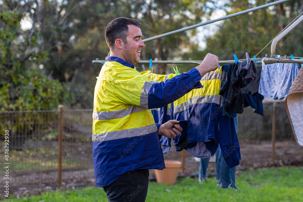 man wearing work shirt pegging clothes onto hills hoist clothesline in ...